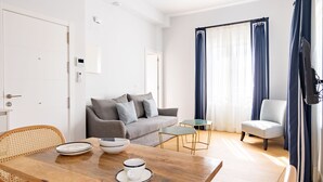Uma sala de estar moderna com uma mesa de jantar de madeira, sofá cinzento e uma pequena mesa redonda.