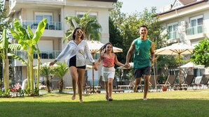 Uma família caminhando em um gramado com uma piscina e cadeiras de sol ao fundo.