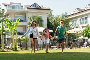 Uma família caminhando em um gramado com uma piscina e cadeiras de sol ao fundo.