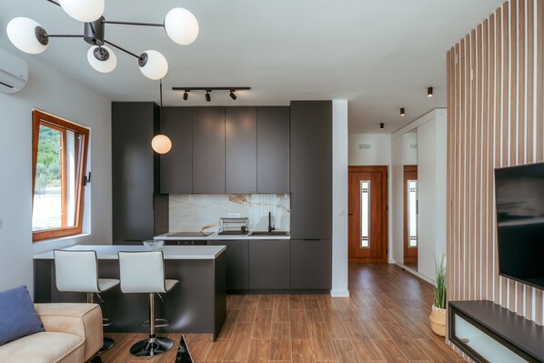 Cozinha moderna com armários escuros, uma ilha central e iluminação pendente.