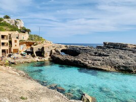 Uma vila costeira com edifícios próximos ao mar, formações rochosas e águas turquesa cristalinas.