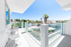 Uma varanda com vista desimpedida para uma piscina, palmeiras e edifícios ao redor.