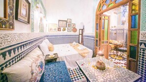 Um interior tradicional marroquino com chão de azulejos estampados, um sofá com almofada decorativa, uma cama com colcha branca e uma mesa com vela.