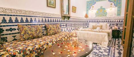Um quarto tradicional marroquino com um sofá estampado, uma mesinha com pétalas de rosa e uma cama com colcha branca.
