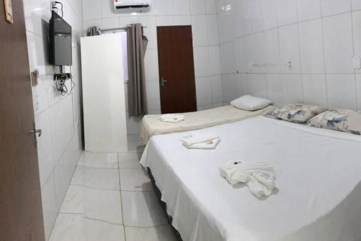 Quarto de hotel com duas camas, uma televisão, uma porta e chão de azulejos.