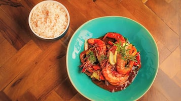 Uma mesa com um prato de camarões e legumes, e uma tigela de arroz.
