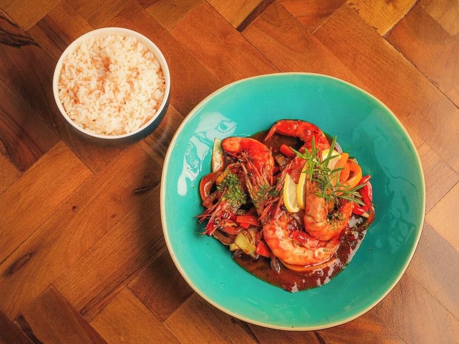 Uma mesa com um prato de camarões e legumes, e uma tigela de arroz.