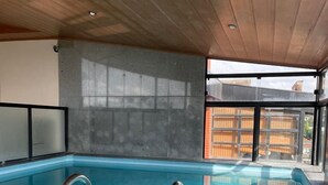 Piscina com grades de metal, chão de azulejos e teto de madeira.