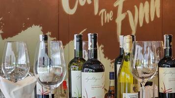 Uma área de bar com garrafas de vinho e copos, com uma placa ao fundo que diz "Cafe at The Fynn".