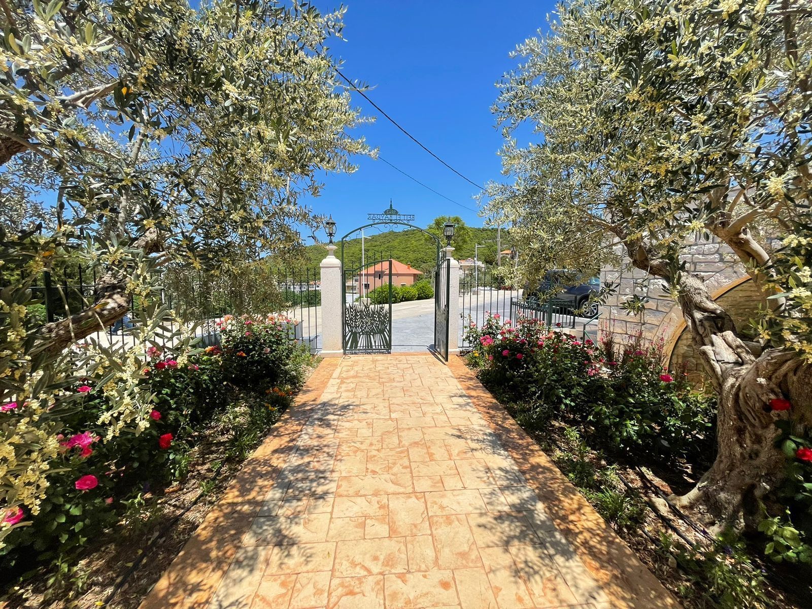 Um caminho pavimentado leva a um portão com vista clara para um edifício ao fundo.