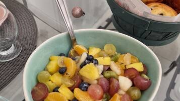 Disposição para o pequeno-almoço com uma tigela de salada de frutas, uma cesta de croissants e um copo de sumo de laranja sobre uma mesa.