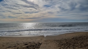 Uma praia com pegadas que levam à água, céu claro e o sol brilhando.