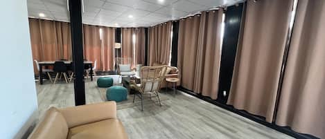 Um quarto espaçoso com uma janela grande, piso de madeira e um espaço de estar com sofá e poltronas.