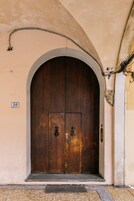 Uma porta de madeira grande com puxador de metal, emoldurada por uma abertura em arco, e uma pequena placa com o número '59' na parede à esquerda.