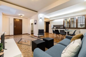 Uma sala de estar moderna com sofá, pufes, televisão de tela plana e um espaço de jantar com cadeiras e mesa.