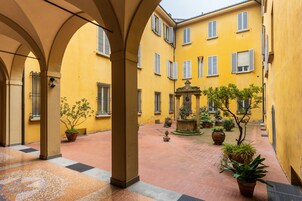 Pátio com edifícios amarelos, arcos e plantas em vasos.