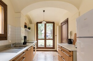 Cozinha com bancadas brancas, armários de madeira, pia dupla e uma janela ampla com vista para o exterior.