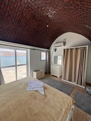 Quarto com uma cama grande, cômoda, espelho e janela com vista para a água.