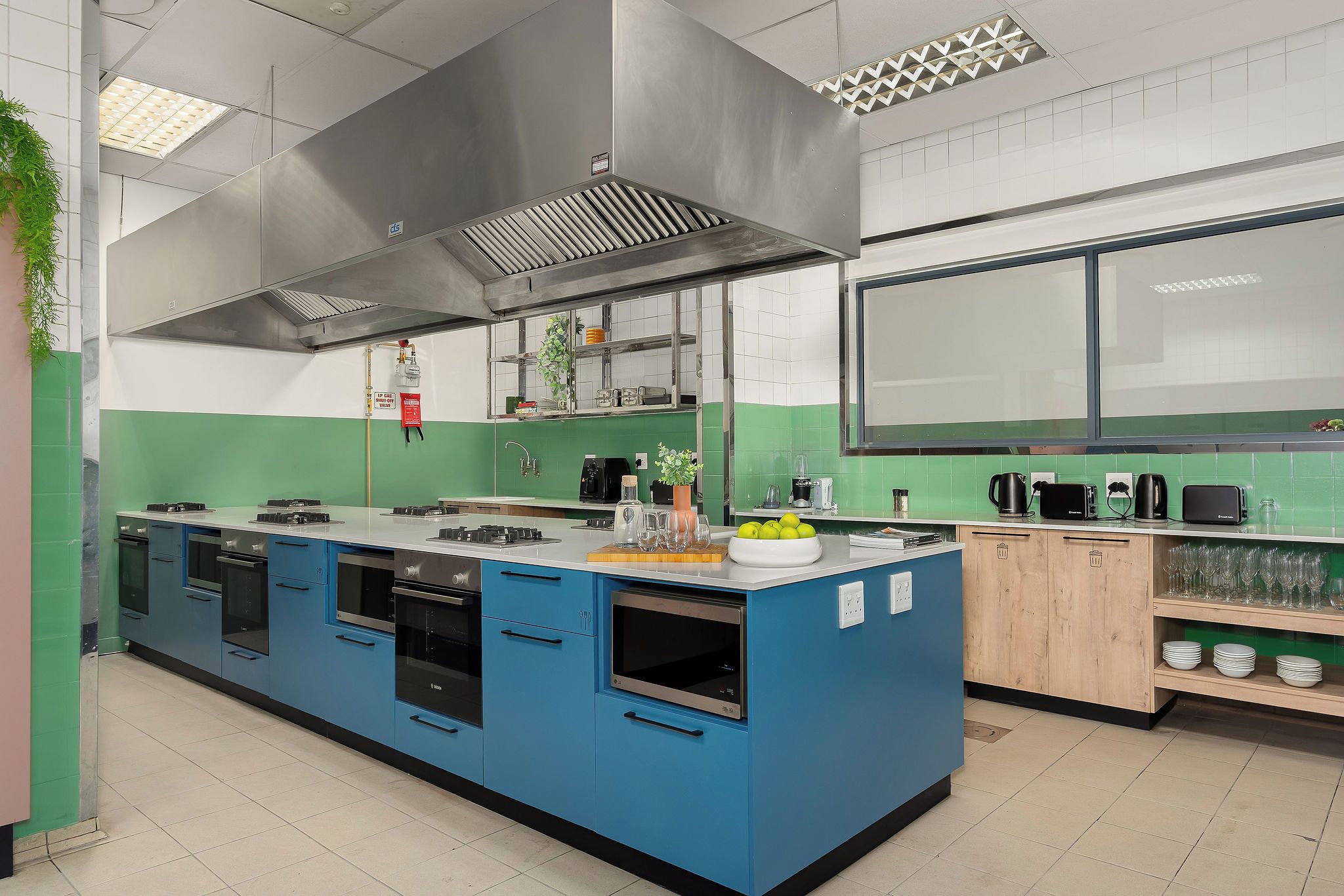 Cozinha comercial com armários azuis, eletrodomésticos de aço inoxidável e uma grande janela.