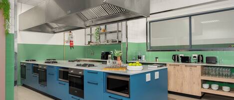 Cozinha comercial com armários azuis, eletrodomésticos de aço inoxidável e uma grande janela.