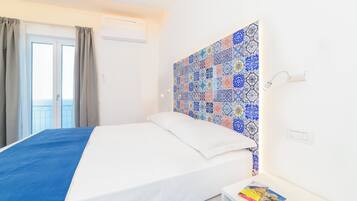Quarto de hotel com cama, mesa de cabeceira, janela com cortinas e parede com design de azulejos estampados.