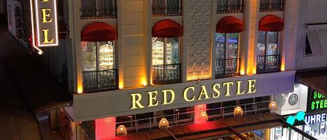 Um hotel com uma placa grande 'HOTEL' e uma inscrição 'RED CASTLE'. Possui áreas de estar ao ar livre e uma placa visível 'STEAKHOUSE'.