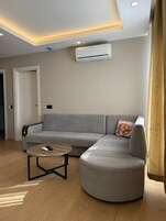 Uma sala de estar moderna com um sofá modular cinza, uma mesa de centro redonda e um aparelho de ar condicionado na parede.