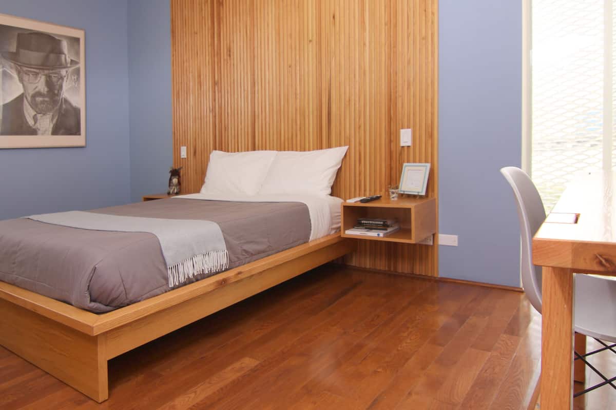 Quarto moderno com estrutura de cama de madeira, mesa de cabeceira com abajur e quadro na parede.