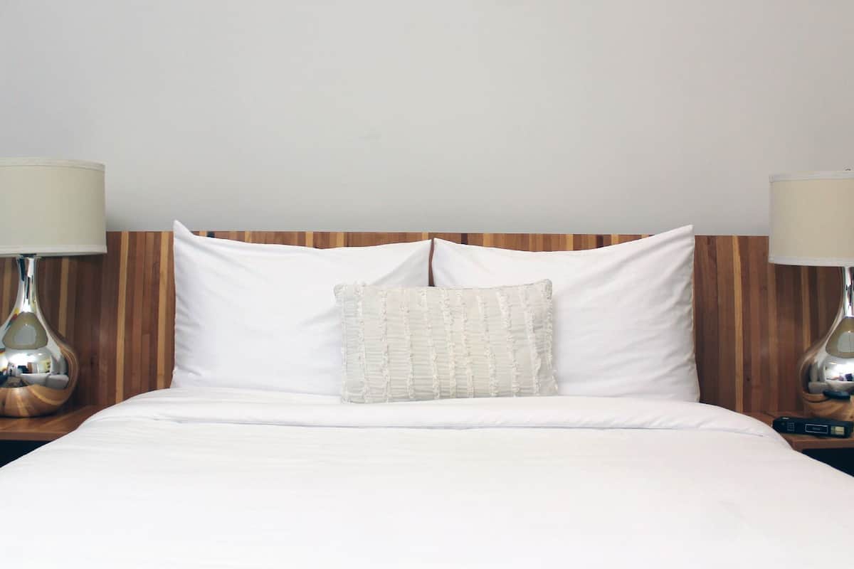Quarto de hotel com cama bem arrumada, duas luminárias de cabeceira e uma cabeceira de madeira.