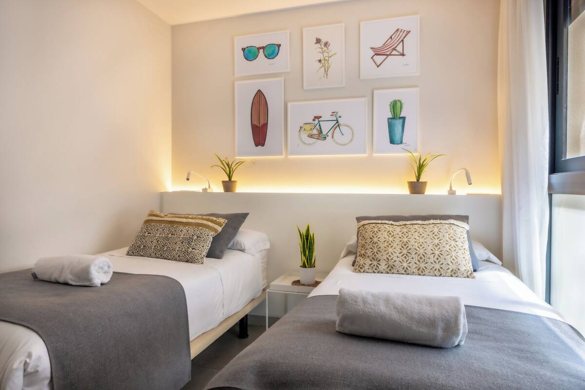 Quarto de hotel com duas camas, uma mesa pequena e uma parede adornada com obras de arte emolduradas.