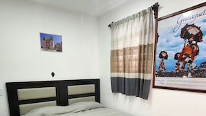 Quarto com cama, um quadro com a imagem de uma dançarina e uma cortina.