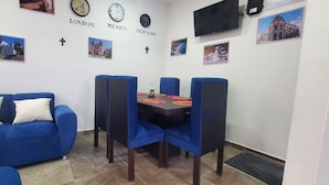 Quarto com um sofá azul, uma mesa de jantar com cadeiras azuis e decorações nas paredes, incluindo relógios e nomes de cidades.
