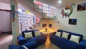 Uma sala de estar com sofá azul, escada com corrimãos coloridos e um mural de uma raposa.