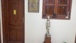 Uma porta de madeira com uma placa de latão, um quadro emoldurado, uma janela com objetos decorativos e uma estátua em um pedestal.