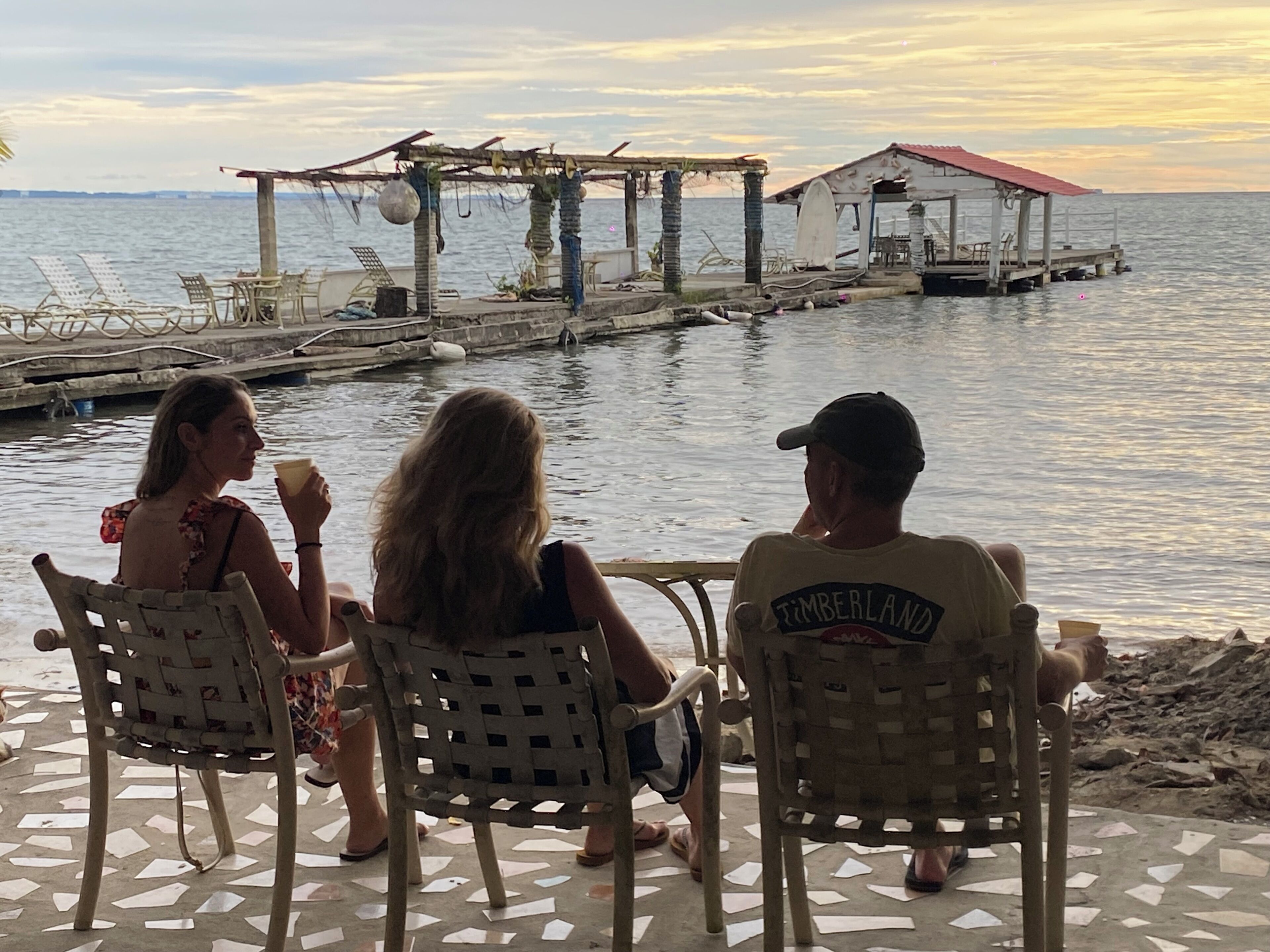 Três pessoas sentadas à mesa com vista para o cais e o mar.