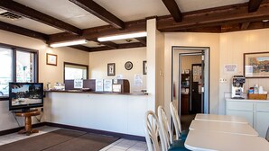 Um restaurante com teto de madeira, uma televisão sobre um suporte de madeira, um balcão com quadros de menu e uma mesa com cadeiras.