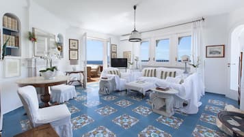 Uma sala de estar espaçosa com uma grande janela com vista para o mar, uma mesa de jantar redonda e um canto aconchegante com um sofá e poltronas.