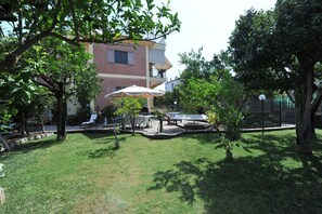 Um pátio com piscina, cadeiras de descanso e um edifício ao fundo.