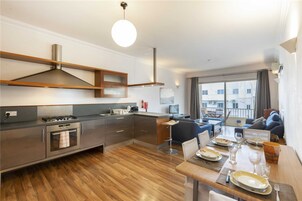 Cozinha moderna com área de jantar, piso de madeira e vista da cidade por grandes janelas.