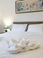 Cama bem arrumada com lençóis brancos e uma toalha dobrada em laço sobre a cama.