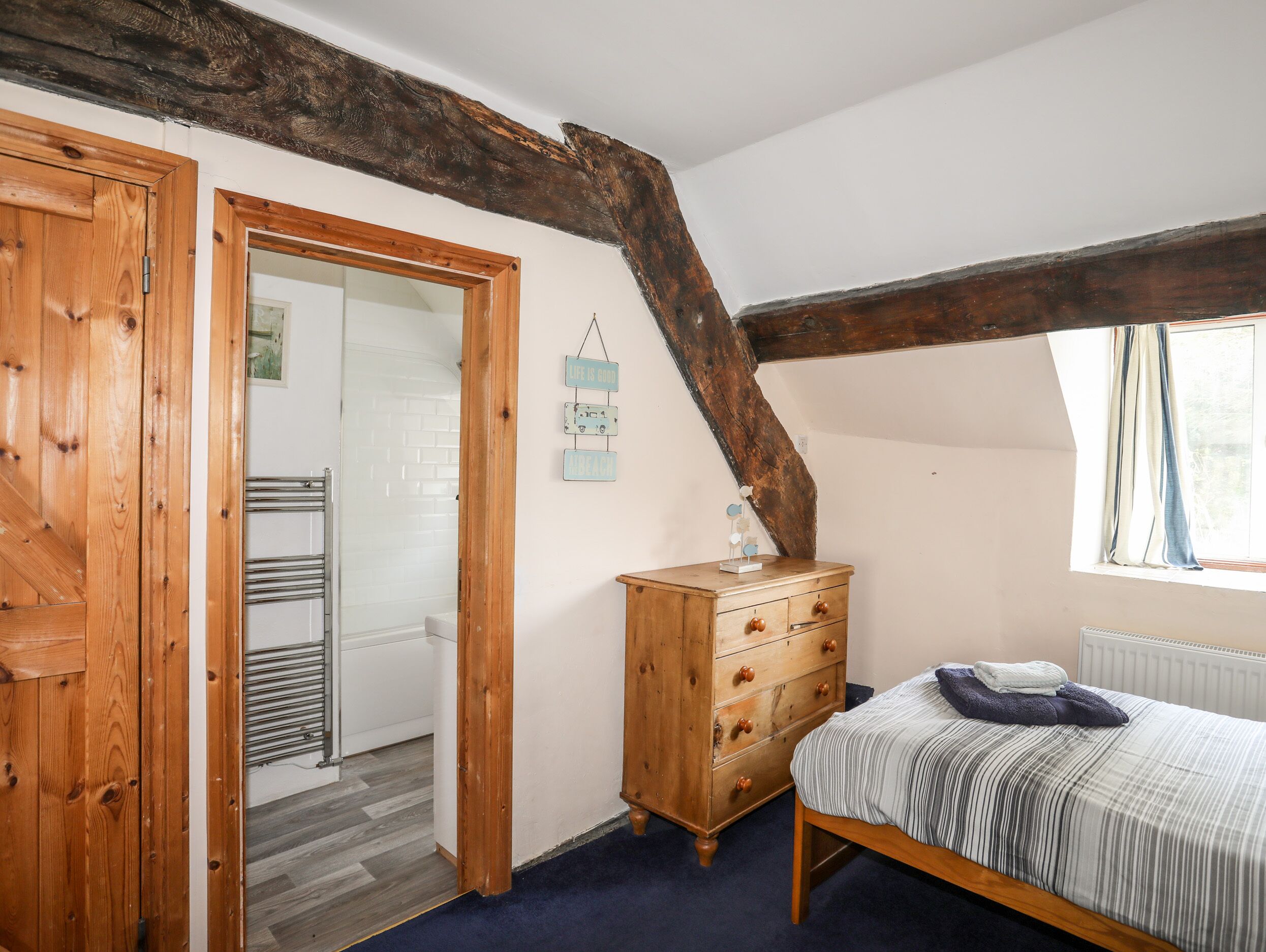 Quarto com armário de madeira, cama com roupa de cama listrada, radiador e janela com cortinas.