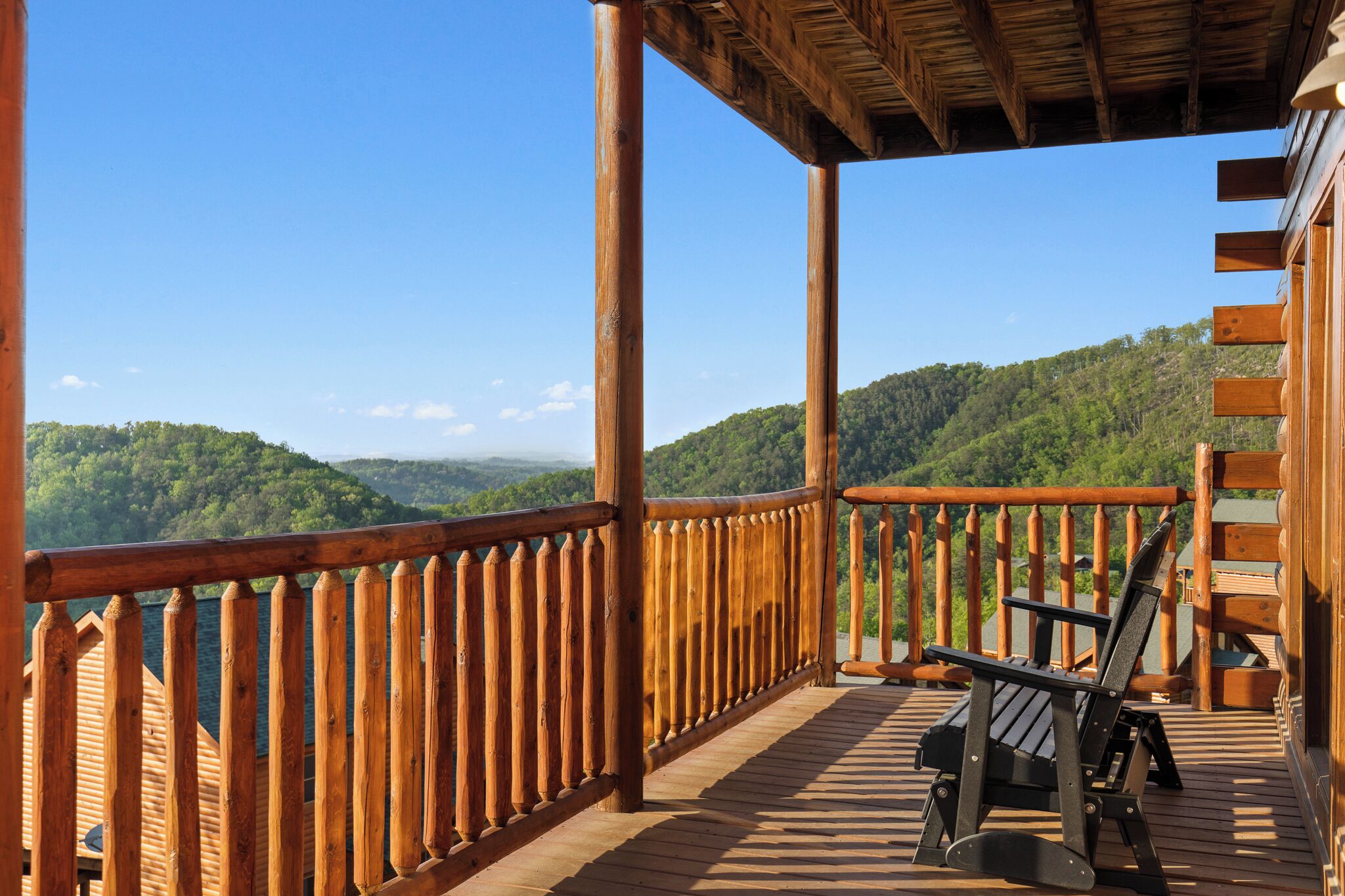 Um deck de madeira com guarda-corpo de madeira, um banco e vista para uma cordilheira arborizada.