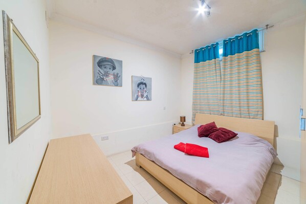 Um quarto com cama, mesa de cabeceira, espelho e duas imagens penduradas na parede.
