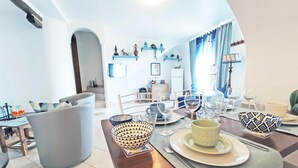 Uma sala de jantar com uma mesa de madeira posta para uma refeição, uma poltrona cinza e uma escadaria que leva a um andar superior.