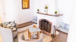 Uma sala de estar com lareira, um sofá, uma poltrona e uma pequena mesa com uma revista.
