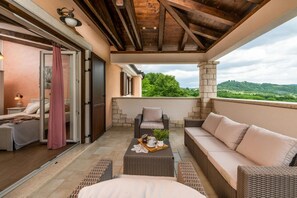 Uma varanda acolhedora com móveis de vime, uma mesinha com bandeja e vista para colinas verdes.