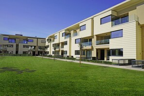Um prédio de apartamentos moderno com várias varandas, um gramado bem cuidado e um céu limpo.