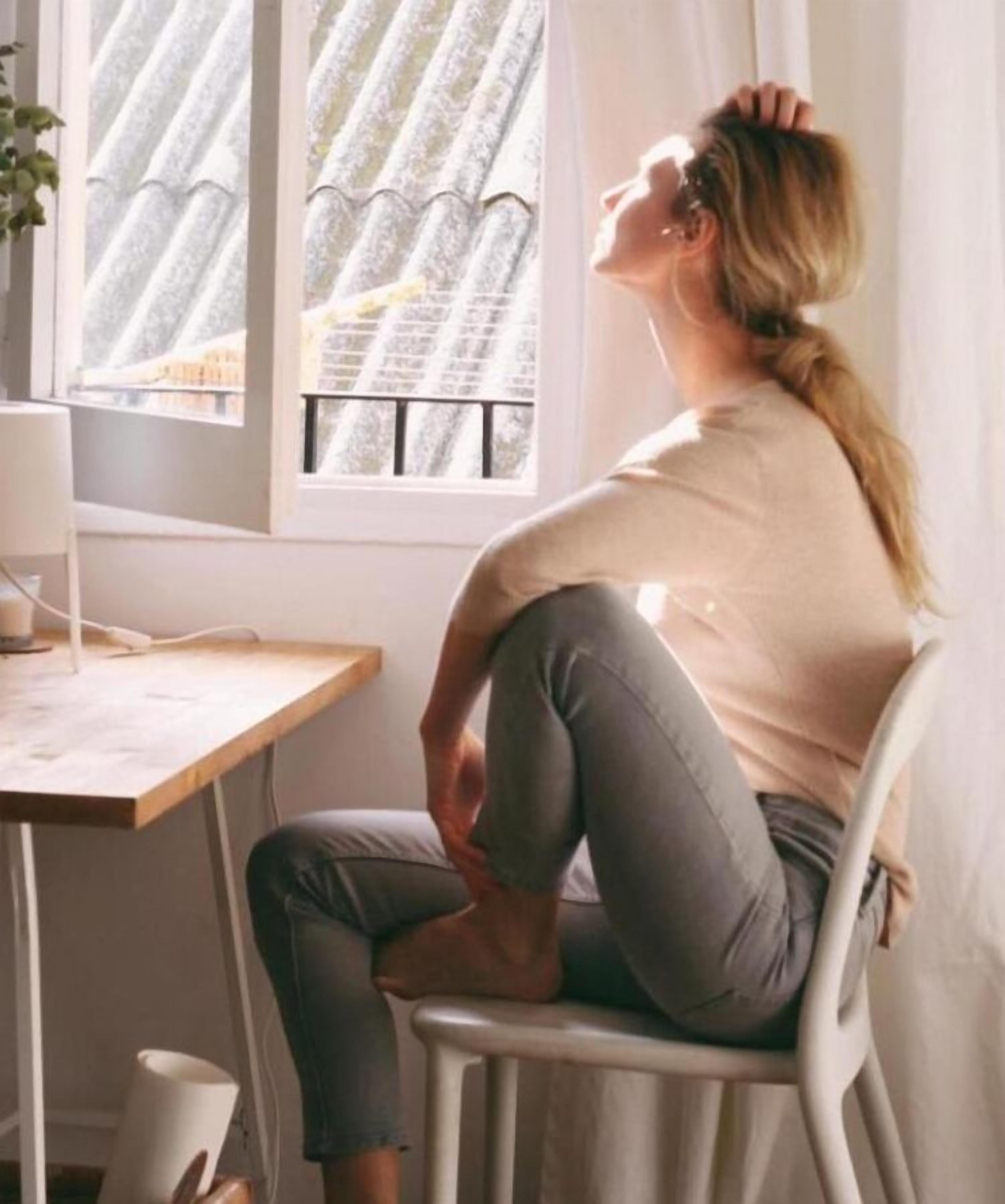 Uma pessoa sentada numa cadeira perto de uma janela, com um computador sobre a mesa.