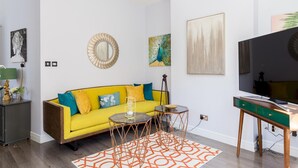 Uma sala de estar moderna com um sofá amarelo, uma mesa de centro de vidro e uma TV em um suporte de madeira.