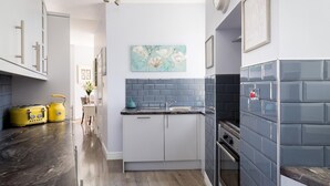 Uma cozinha estreita com armários brancos, painel azul e uma pequena ilha. Há dois eletrodomésticos amarelos na bancada.